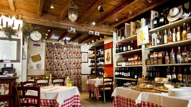 Interior de restaurante com vigas de madeira, toalhas de mesa xadrez e prateleiras cheias de garrafas.