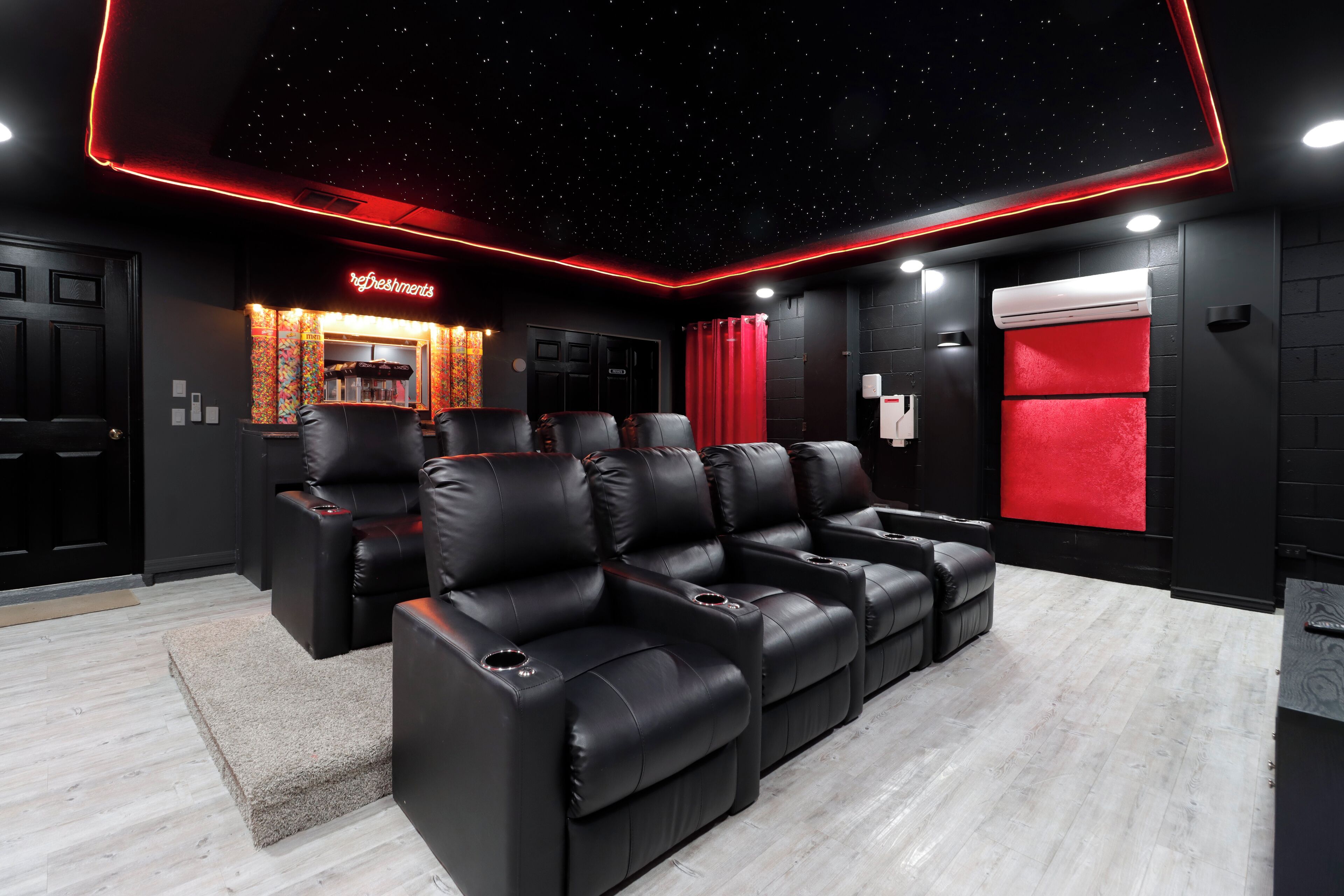 Sala de cinema com poltronas reclináveis de couro preto, uma cortina vermelha e design de teto com estrelas.