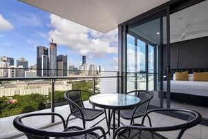 Quarto de hotel moderno com varanda, parede de vidro e vista para a cidade.