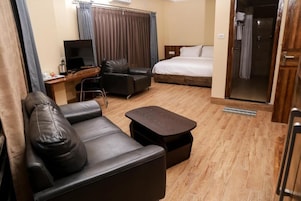 Quarto de hotel com sofá de couro, uma secretária pequena com televisão, uma cama e área de chuveiro.