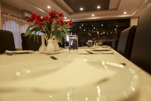 Mesa de jantar posta com toalha branca, flores vermelhas e copos de vidro transparente.