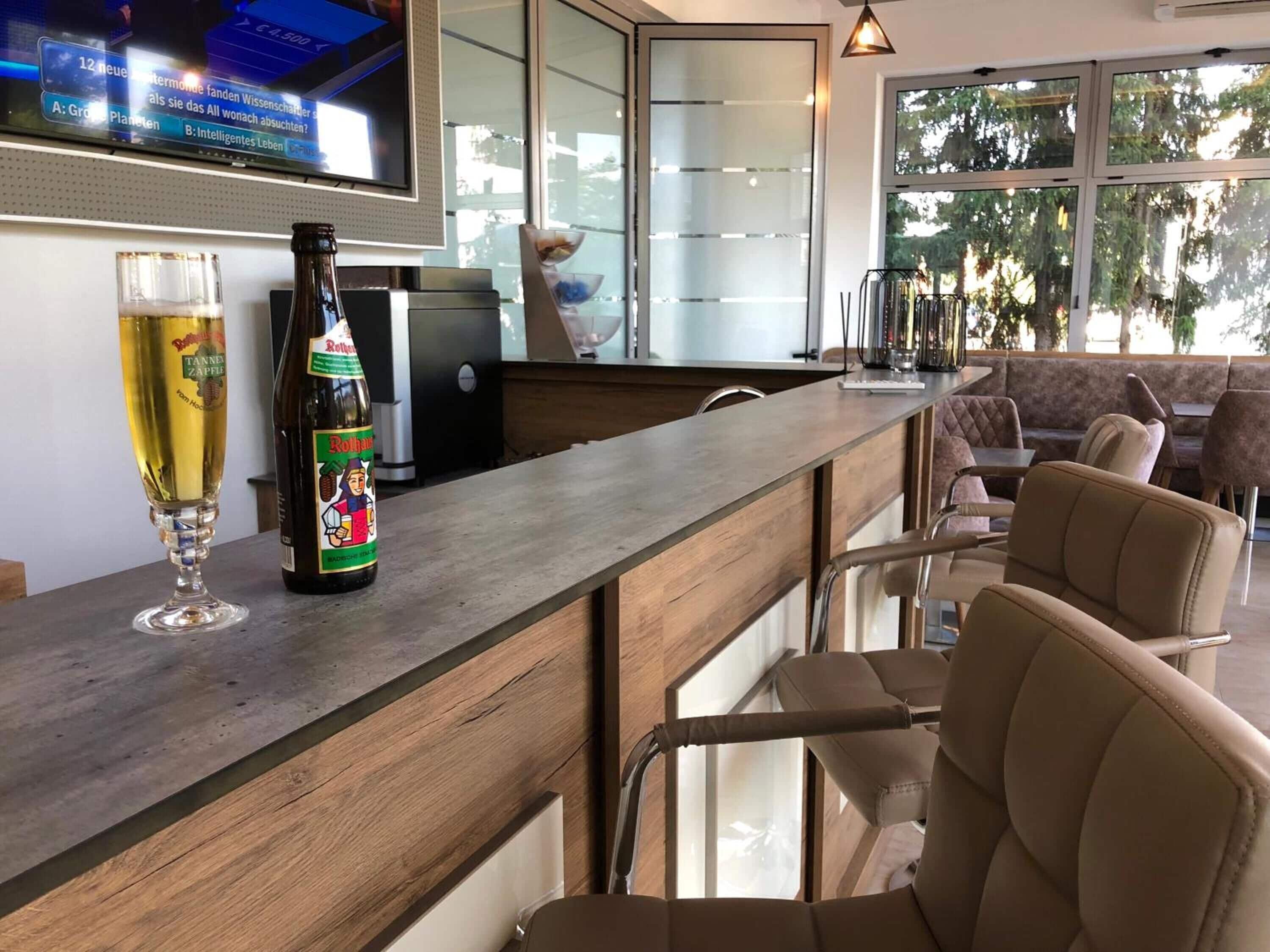 Uma área de bar com balcão de madeira, uma garrafa de cerveja e um copo de cerveja.