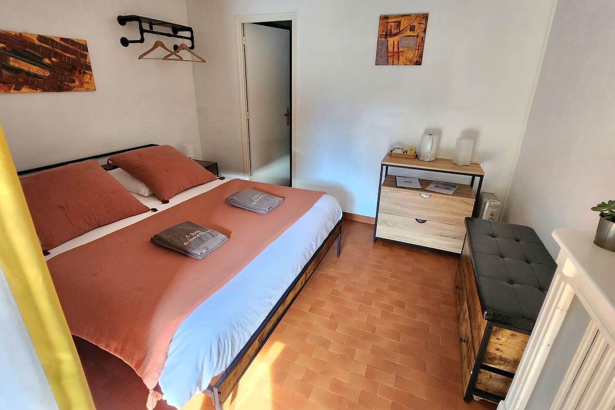 Um quarto com uma cama, mesa de cabeceira, cadeira e porta.