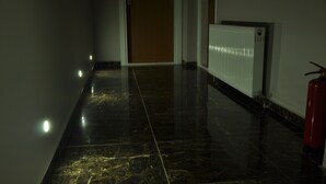 Um corredor com chão de mármore preto brilhante, um radiador branco e um extintor de incêndio vermelho.