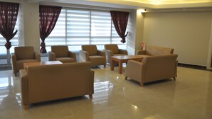 Ampla sala de estar com vários sofás e uma mesa de centro, janelas grandes com cortinas e um design moderno e elegante.