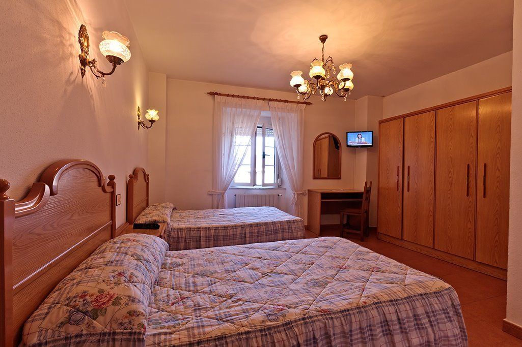 Quarto com duas camas, guarda-roupa de madeira, televisão e um candeeiro.