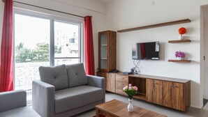 Uma sala de estar moderna com um sofá cinzento, um armário de madeira e uma TV na parede.
