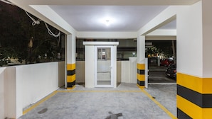 Entrada de um estacionamento com porta branca, defensa com listras amarelas e pretas e piso de concreto.