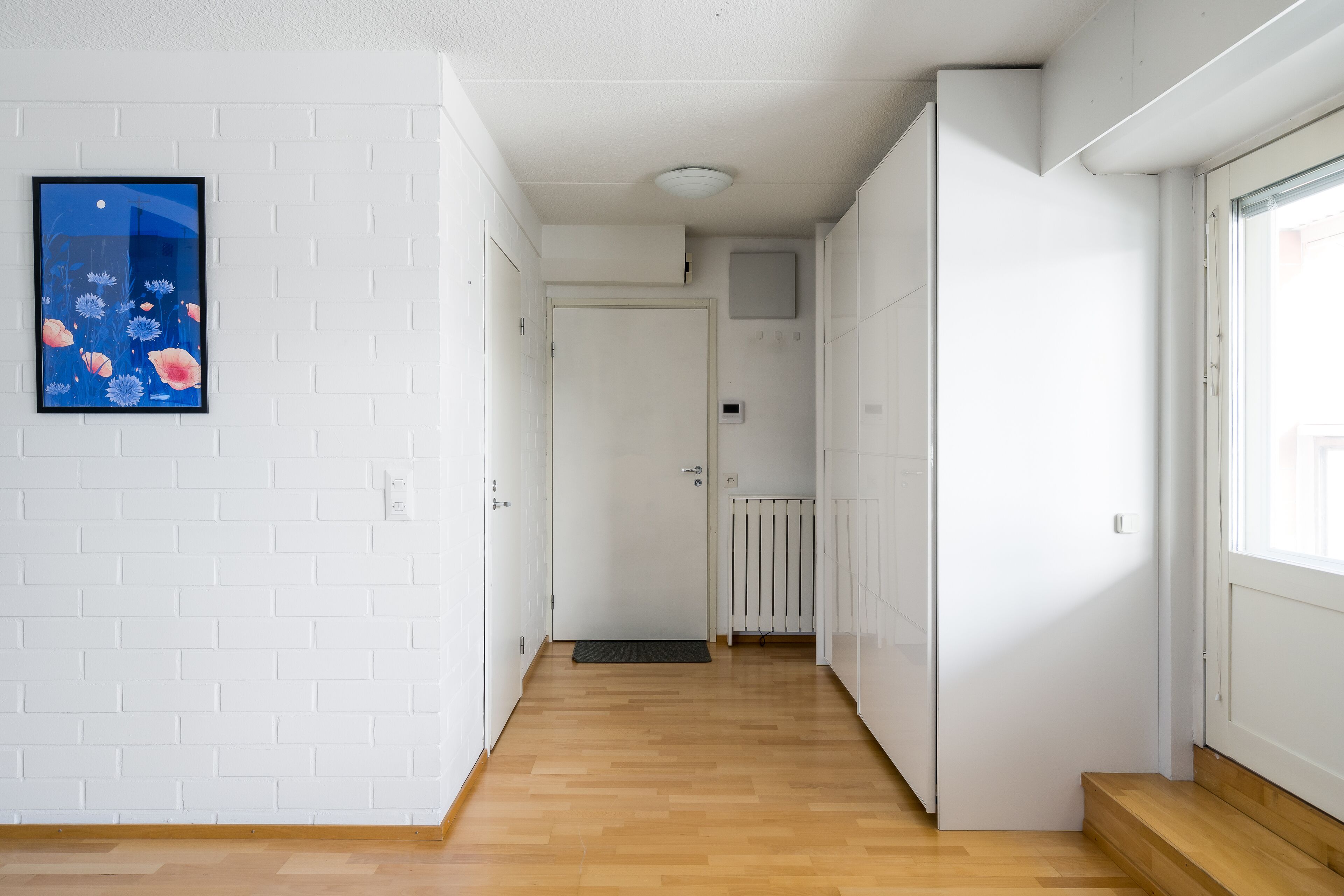 Corredor com paredes de tijolo branco, piso de madeira e uma porta no final.