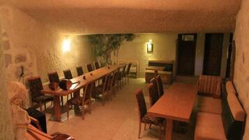 Uma sala de jantar com uma mesa de madeira comprida e cadeiras, um sofá e uma mesinha com abajur.