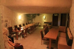 Uma sala de jantar com uma mesa de madeira comprida e cadeiras, um sofá e uma mesinha com abajur.