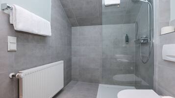 Uma casa de banho moderna com cabine de duche em vidro, sanita branca e radiador branco.