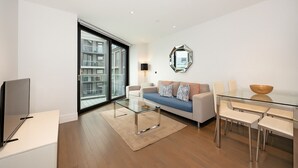 Uma sala de estar moderna com uma mesa de centro de vidro, um sofá com almofadas, uma mesa de jantar com cadeiras e uma janela grande com vista para um edifício.