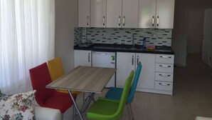Uma cozinha compacta com armários brancos, bancada preta e uma pequena área de refeições com mesa de madeira e cadeiras coloridas.