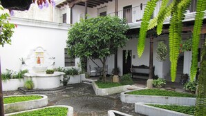 Um pátio com caminhos de pedra, plantas em vasos e um edifício branco com uma fonte.