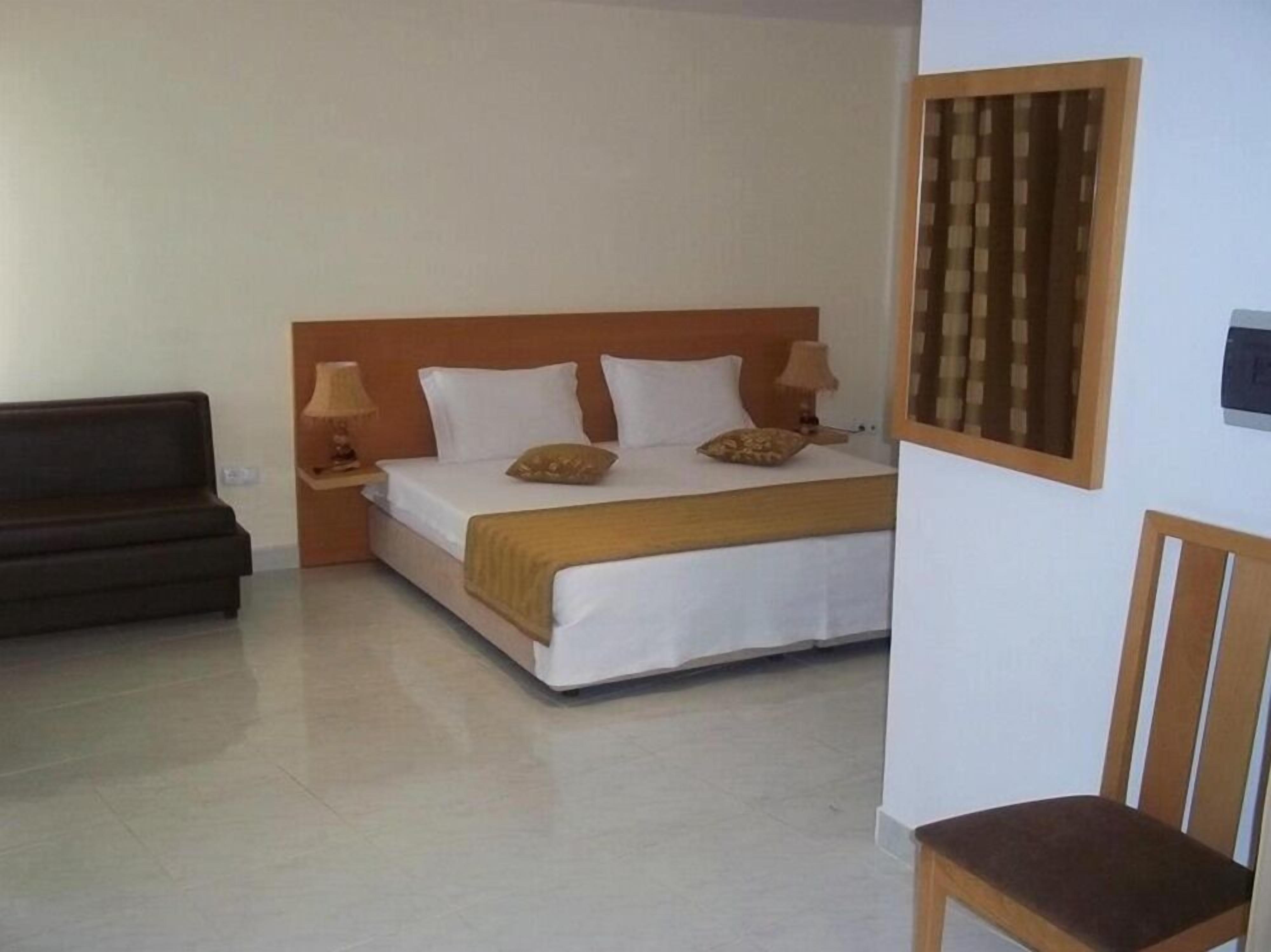 Quarto de hotel com cama, abajures, cabeceira de madeira, uma cadeira e luminária na parede.