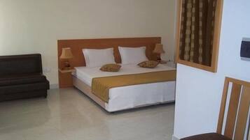 Quarto de hotel com cama, abajures, cabeceira de madeira, uma cadeira e luminária na parede.