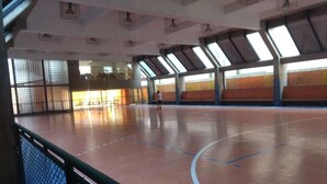 Um ginásio coberto com quadra de basquete, grandes janelas e teto alto.