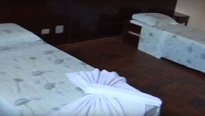 Quarto de hotel com duas camas, soalho de madeira e um guarda-roupa de cor escura.