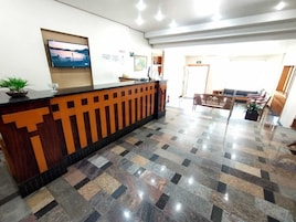 Uma área de recepção com balcão de check-in, uma televisão fixada na parede e um chão com padrão.