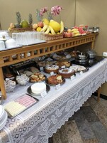Disposição de buffet com diversos alimentos e uma toalha de mesa decorativa.