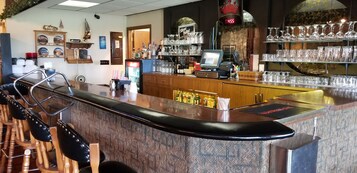 Uma área de bar com balcão, cadeiras e prateleiras cheias de copos.