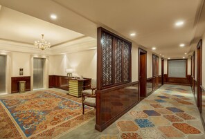 Um corredor amplo com carpete estampado, painéis de madeira e um candelabro.