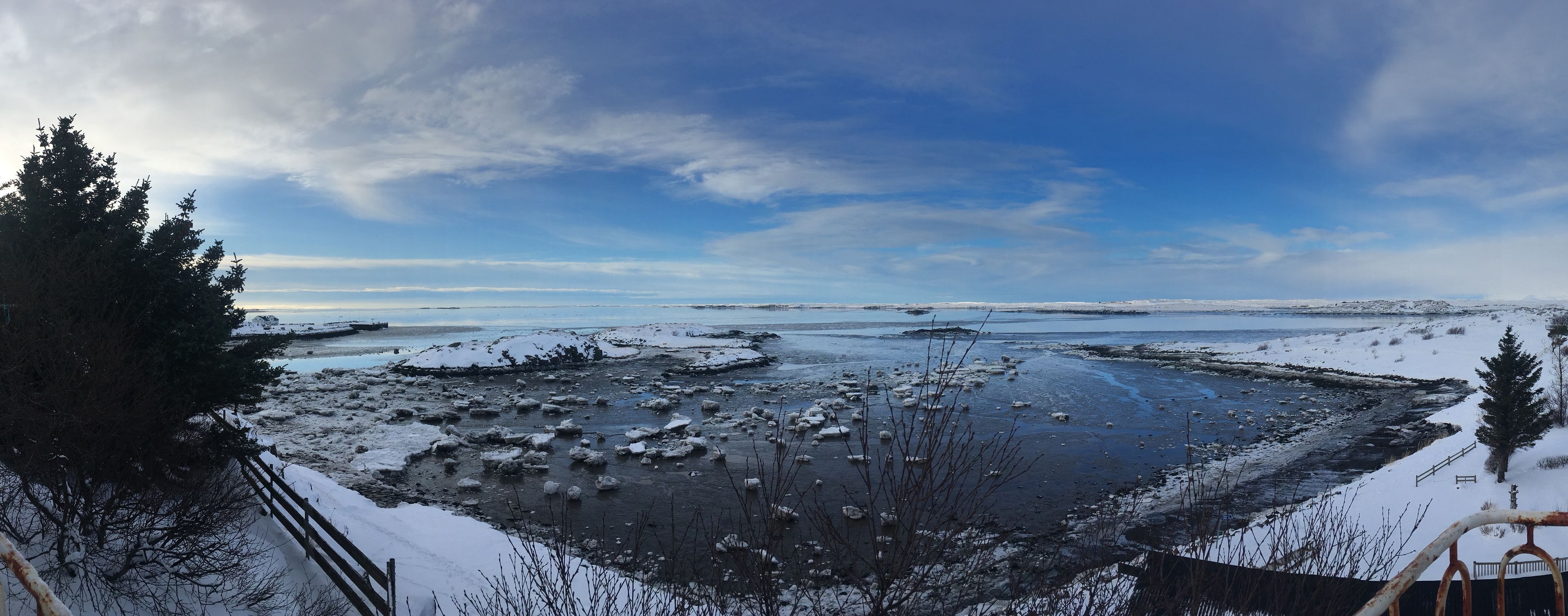 Vista panorâmica de uma paisagem nevada com um rio congelado, árvores ao longe e céu claro.