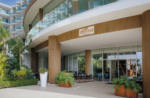 Um bistrô moderno com mesas ao ar livre, grandes janelas e uma placa com a inscrição 'theros BISTRO'.
