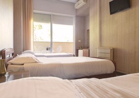 Quarto de hotel com duas camas, uma escrivaninha, uma cadeira, um radiador e uma televisão na parede.