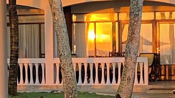 Exterior de hotel com varanda branca, palmeiras e vista para o pôr do sol.