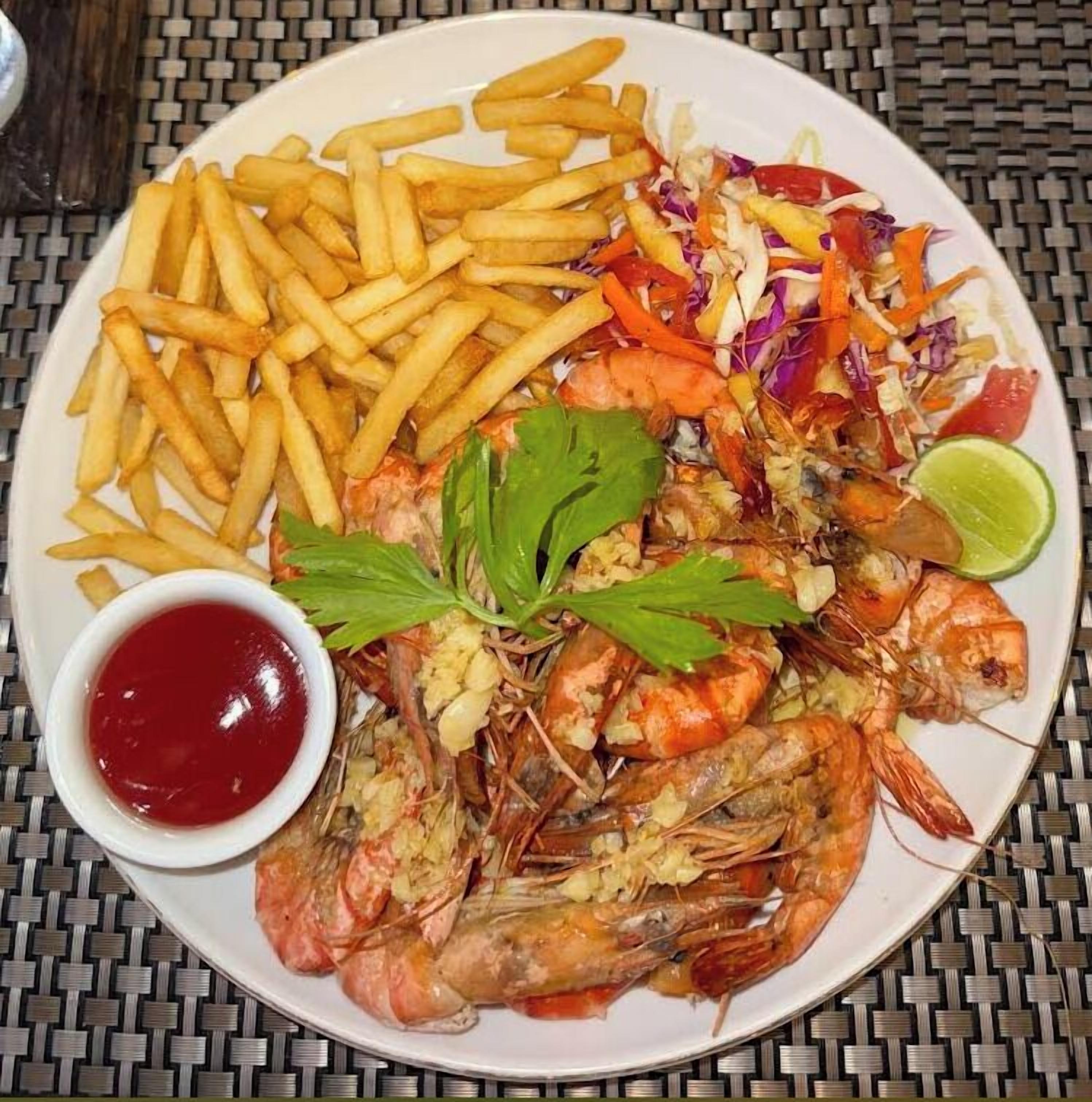 Um prato de comida com camarão, batatas fritas, salada e ketchup acompanhando.