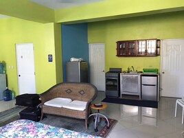 Quarto de hotel compacto com uma cama, um sofá de vime, uma cozinha compacta e um banheiro.