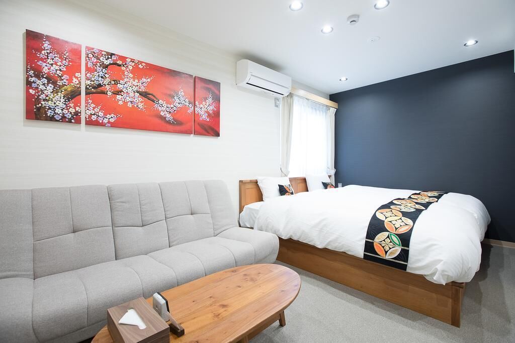 Quarto de hotel com cama, sofá, mesa de cabeceira de madeira e duas unidades de ar condicionado fixadas na parede.