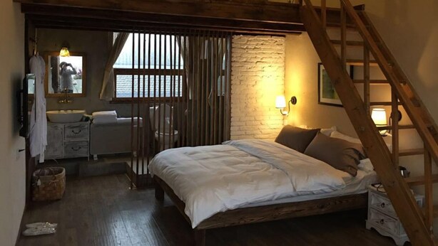 Quarto com beliche, escada de madeira, banheiro pequeno com espelho e janela com cortinas.