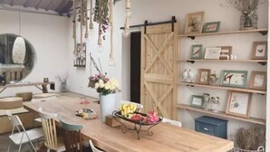 Uma área de refeições com mesa de madeira, cadeiras, plantas pendentes e uma prateleira na parede com quadros.