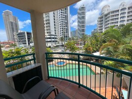 Varanda com vista para uma piscina, cercada por palmeiras e edifícios modernos.