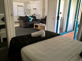 Quarto de hotel com uma cama, um sofá, uma mesa de centro e uma cozinha compacta ao fundo.