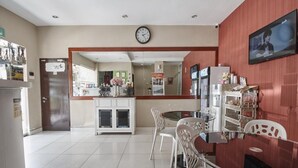Uma cozinha moderna com armários brancos, uma mesa de jantar com cadeiras, um relógio na parede e uma TV fixada na parede.