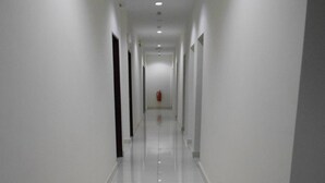 Um corredor comprido e estreito, com paredes brancas e chão brilhante, que termina numa porta.