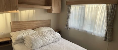 Quarto com cama, cabeceira de madeira, mesas de cabeceira e uma janela com cortinas.