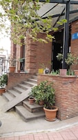 Um edifício de tijolos com entrada coberta, degraus que levam a uma porta e vários vasos de plantas na área da entrada.