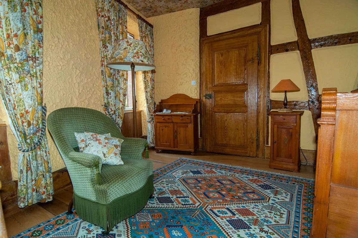 Quarto tradicional com poltrona verde, guarda-roupa de madeira e cortinas estampadas.