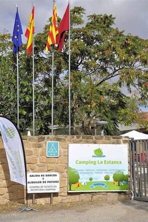 Placa para Camping La Estanca com bandeiras, um muro de pedra e um banner.