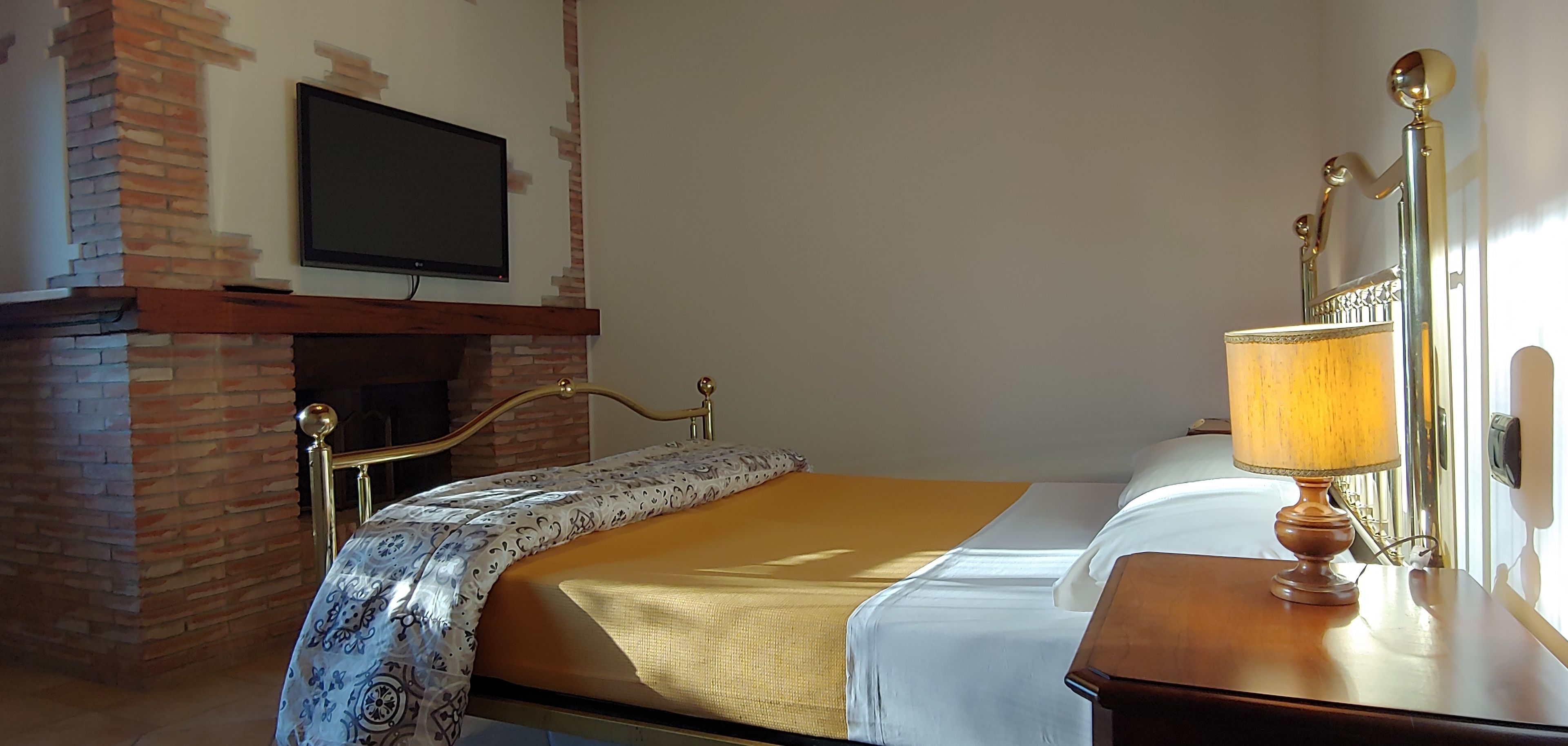 Quarto de hotel com uma cama, televisão na parede, lareira e mesa de cabeceira com abajur.