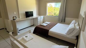 Quarto de hotel com cama, escrivaninha, televisão e janela com cortinas.