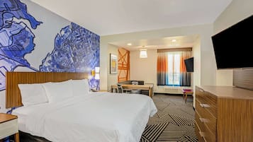 Quarto de hotel com uma cama grande, uma escrivaninha, uma cadeira, uma televisão e um tapete estampado.
