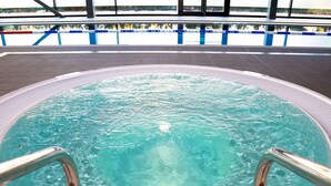 Uma banheira de hidromassagem com grades de metal, cercada por um deck revestido e uma piscina com marcações de pistas.