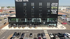 Um edifício com uma placa indicando 'VILLAGE HOTEL' e 'JOIN VILLAGE GYM HEALTH CLUB + POOL'.
