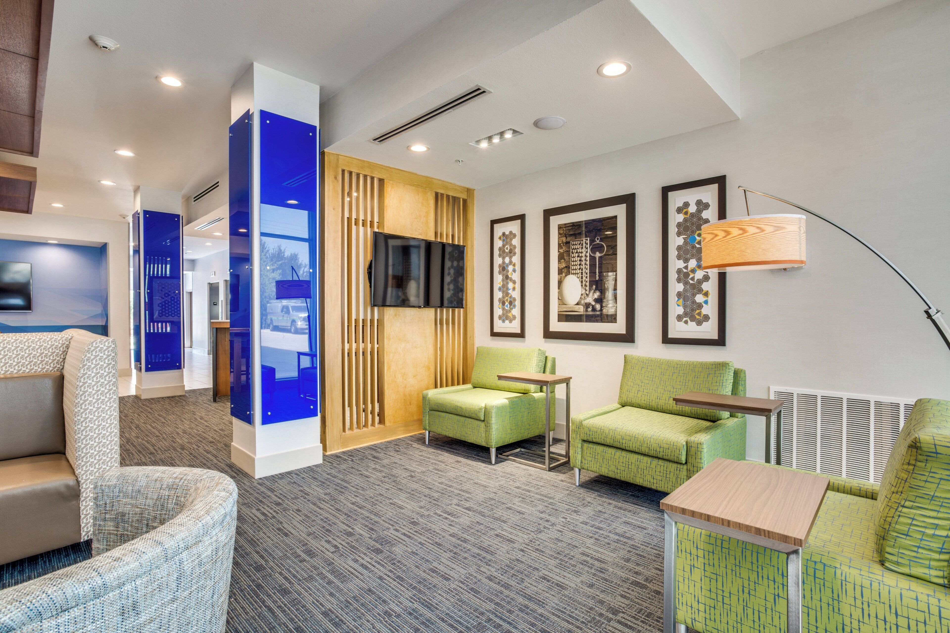 Um hall de hotel com áreas de estar, uma televisão de tela plana, obras de arte emolduradas e design moderno.